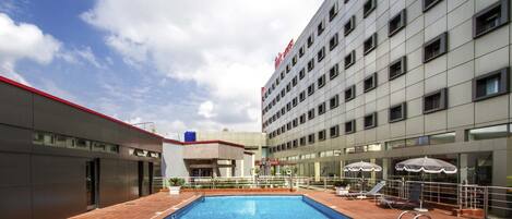 Um hotel com piscina interna, um edifício de telhado vermelho e uma fachada moderna.