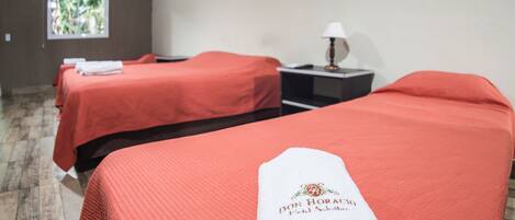 Quarto de hotel com duas camas, uma janela, um ar condicionado e um abajur em uma mesa de cabeceira.