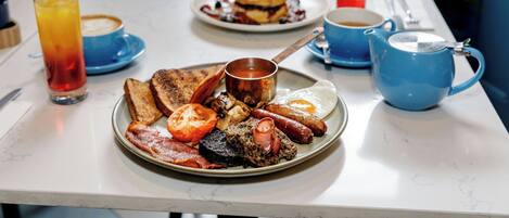 Prato de café da manhã com torradas, bacon, ovos, linguiça e um pequeno pote de geleia.