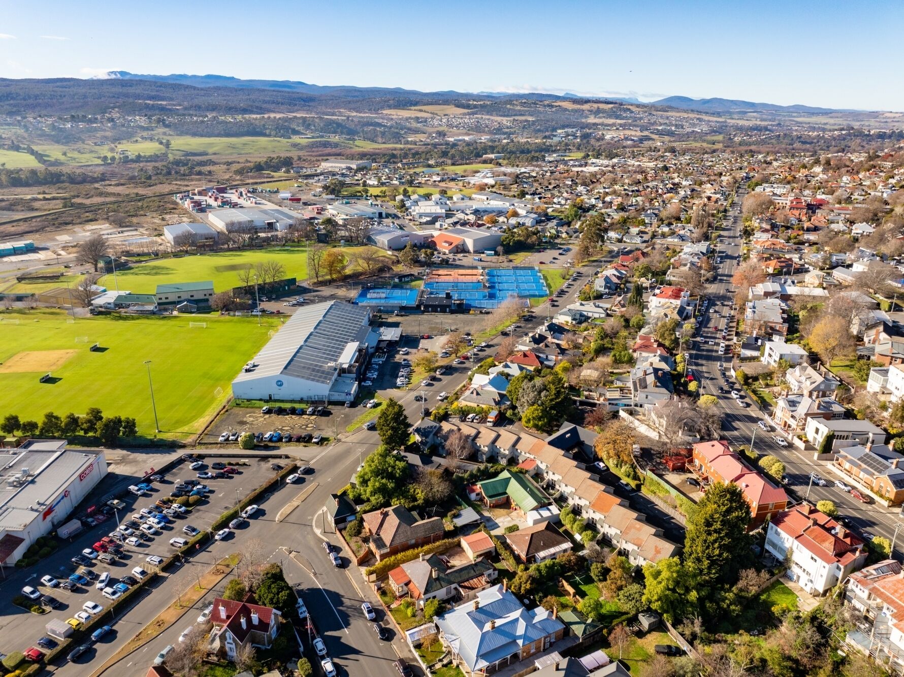 Vista aérea de uma cidade com uma extensa área industrial, casas residenciais e um campo verde.