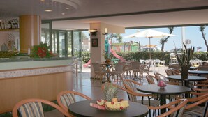 Um saguão de hotel com área de bar, espaço para sentar ao ar livre e vista para a praia.
