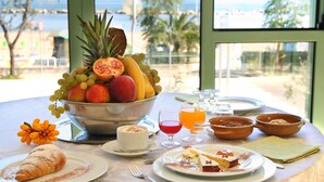 Mesa de café da manhã com uma fruteira, croissant e pratos de comida, com vista panorâmica.