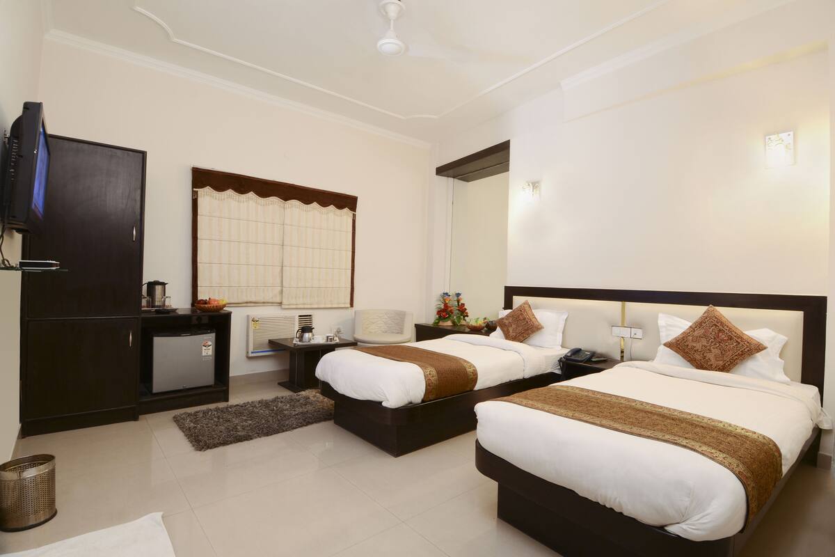 Quarto de hotel com duas camas, uma televisão, uma escrivaninha e uma kitchenette pequena.