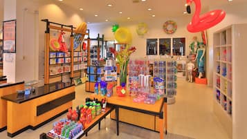 Loja bem iluminada com prateleiras cheias de brinquedos e acessórios coloridos, uma grande decoração de flamingo e uma vitrine com diversos itens, incluindo um enfeite em formato de abacaxi.