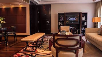 Um hall de hotel moderno com um sofá, um banco, uma mesa de jantar e uma televisão exibindo "LIVE LIFE TO DISCOVER".