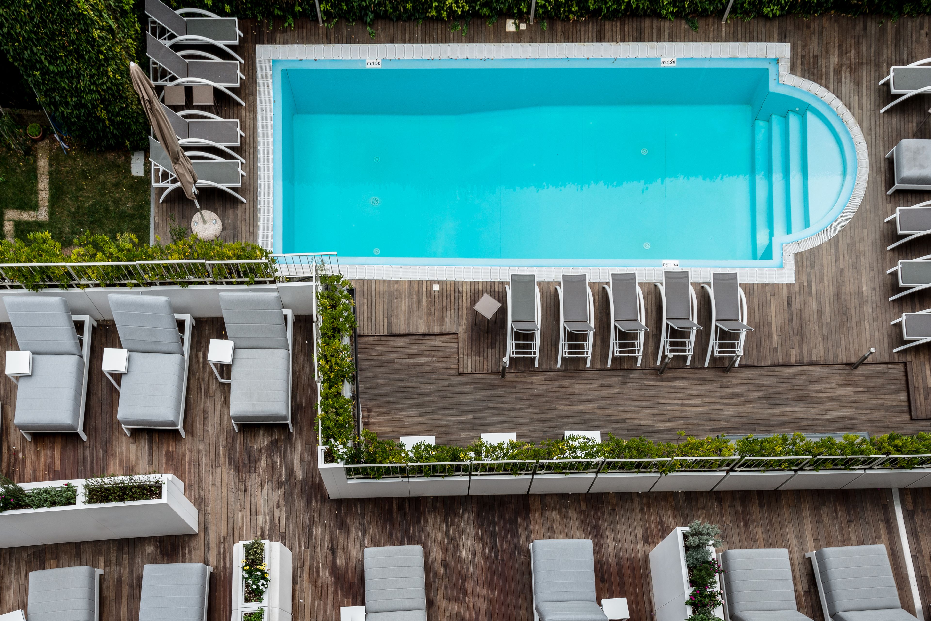Vista aérea de uma área de piscina no terraço, com piscina retangular, espreguiçadeiras e deck de madeira.