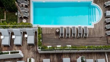 Vista aérea de uma área de piscina no terraço, com piscina retangular, espreguiçadeiras e deck de madeira.