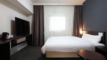 Quarto de hotel com uma cama, televisão, mesa de cabeceira, abajur e janela com cortinas.