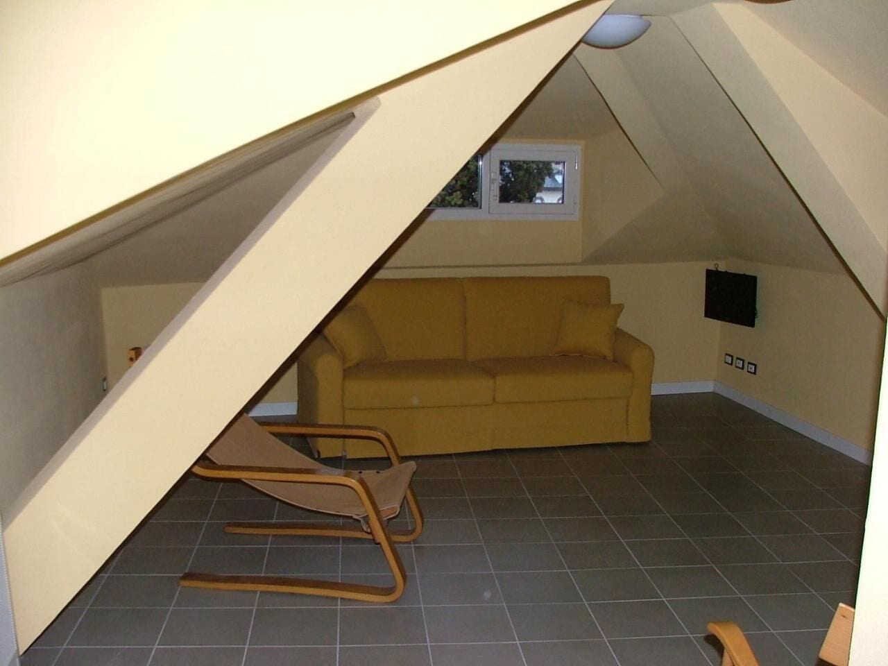 Um quarto de sótão com um sofá castanho, uma cadeira de madeira e uma janela.
