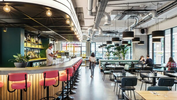 Uma área de bar moderna com balcão curvo, assentos para clientes e um barista visível.