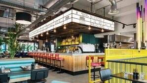 Uma área de bar com banquetas, balcão e espaço para sentar com mesas e cadeiras.