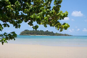 Uma praia com águas turquesa cristalinas, uma faixa de areia e uma ilha arborizada ao longe.