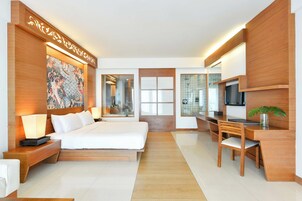 Quarto de hotel moderno com uma cama grande, uma escrivaninha, uma cadeira, uma TV e um objeto decorativo na parede.