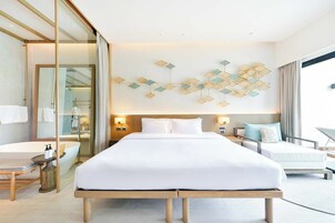 Quarto de hotel com cama grande, área de estar separada, banheira e um objeto decorativo fixado na parede.