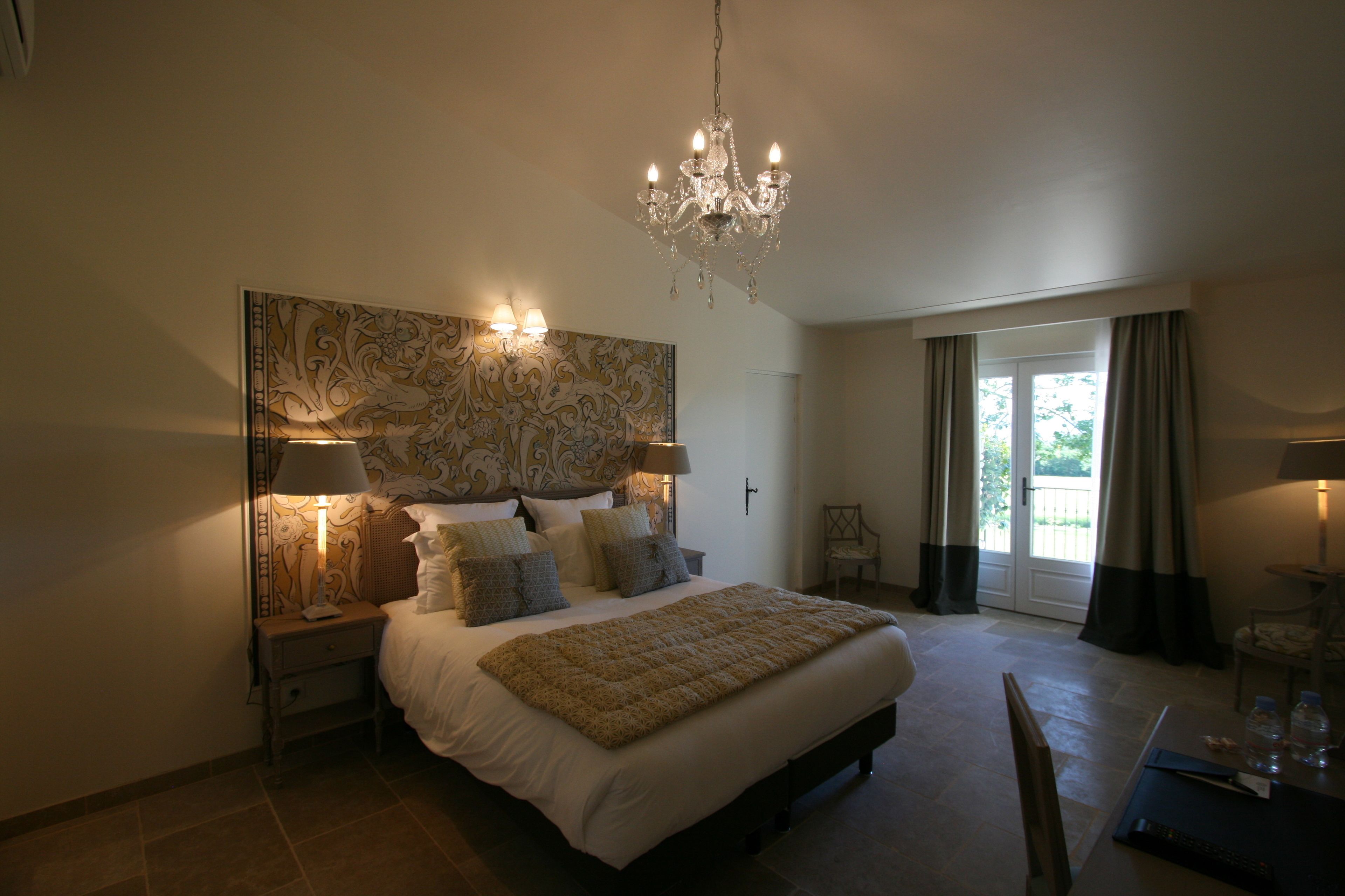 Quarto com cama grande, um lustre e vista para o exterior por uma porta deslizante.