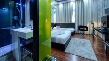 Quarto de hotel moderno com box de vidro, cama grande, mesa de cabeceira e televisão.