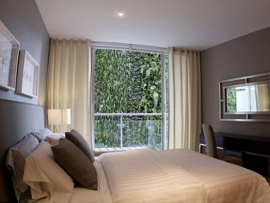 Quarto de hotel com uma cama, uma escrivaninha, uma cadeira, janela com cortinas e quadros nas paredes.