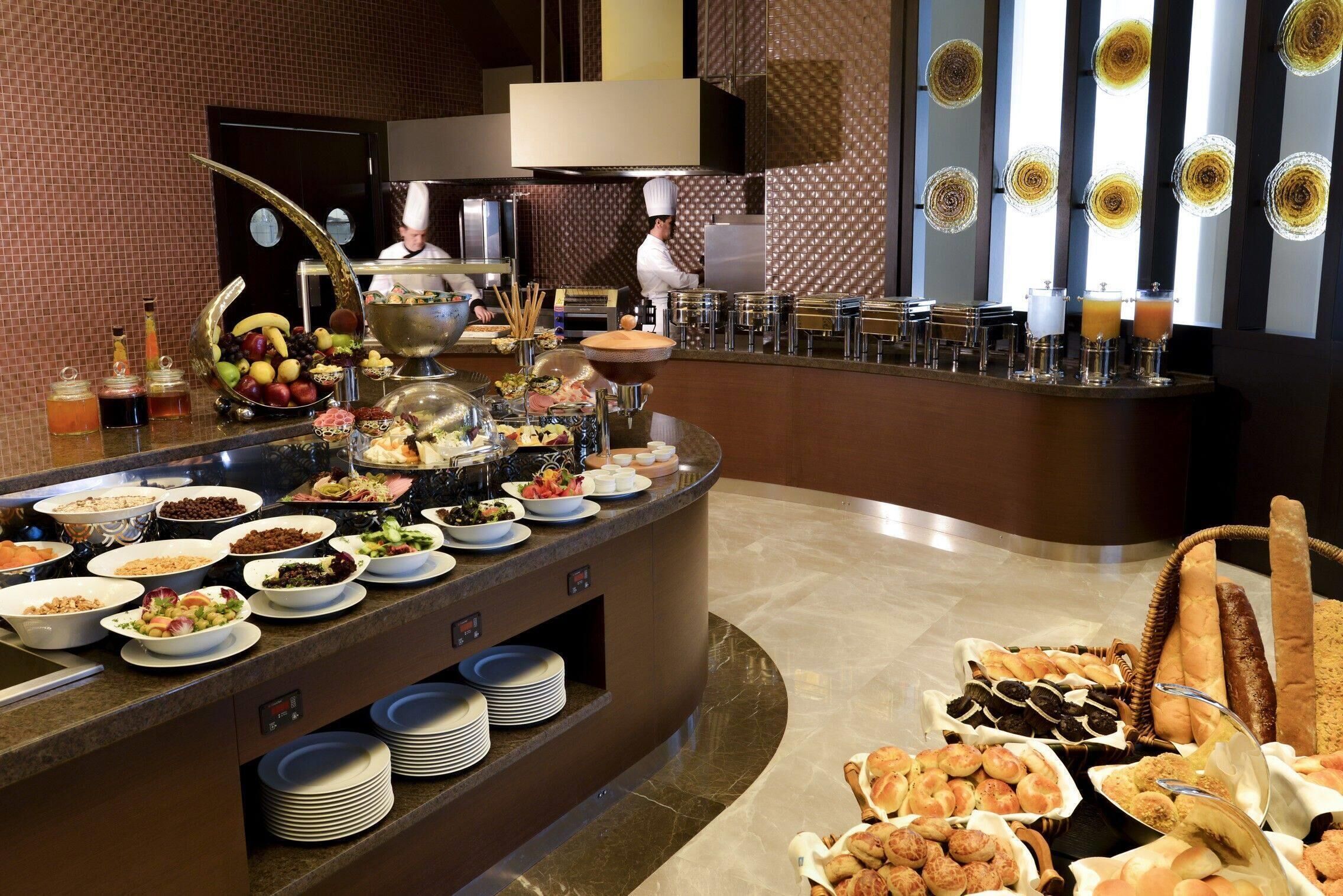 Buffet com diversas opções de comida e um cozinheiro ao fundo.