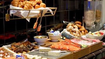 Buffet com diversos itens, incluindo pães, carnes, queijos e frutas.