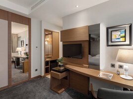 Quarto de hotel moderno com uma escrivaninha de madeira, televisão de tela plana, um espelho grande e uma pintura abstrata emoldurada.