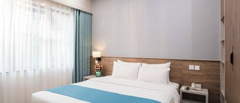 Quarto de hotel com uma cama grande, mesa de cabeceira com abajur e cabeceira de madeira.