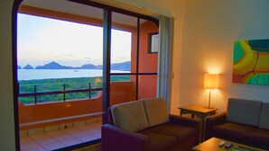 Quarto com sofá, mesa de centro e vista para um corpo de água e montanhas.