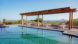 Piscina límpida com espreguiçadeiras e um pergolado, com vista para uma paisagem deslumbrante.