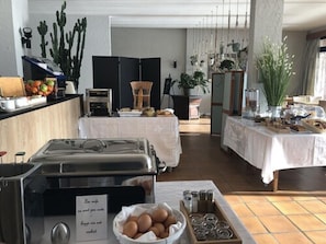 Disposição de buffet de café da manhã com diversos alimentos e uma placa indicando o horário do serviço.