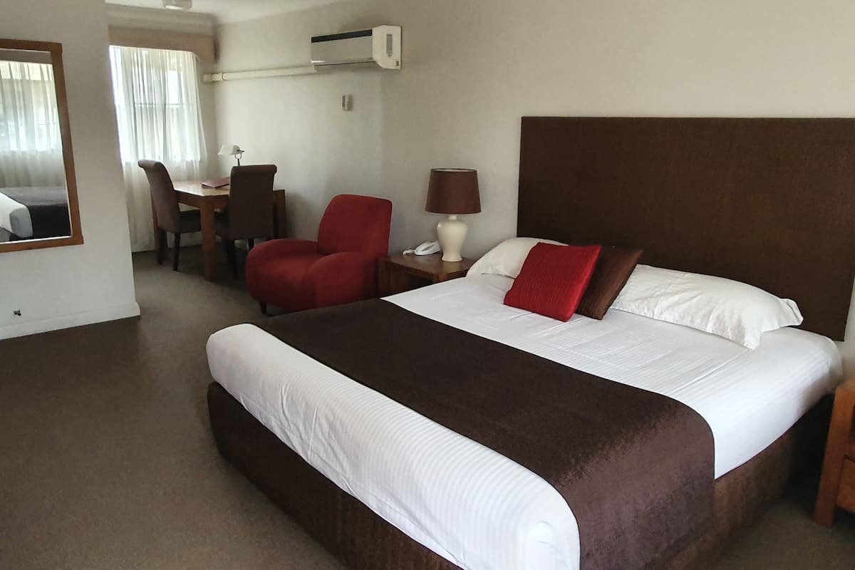 Quarto de hotel com uma cama grande, uma escrivaninha, uma cadeira, um abajur e um espelho.