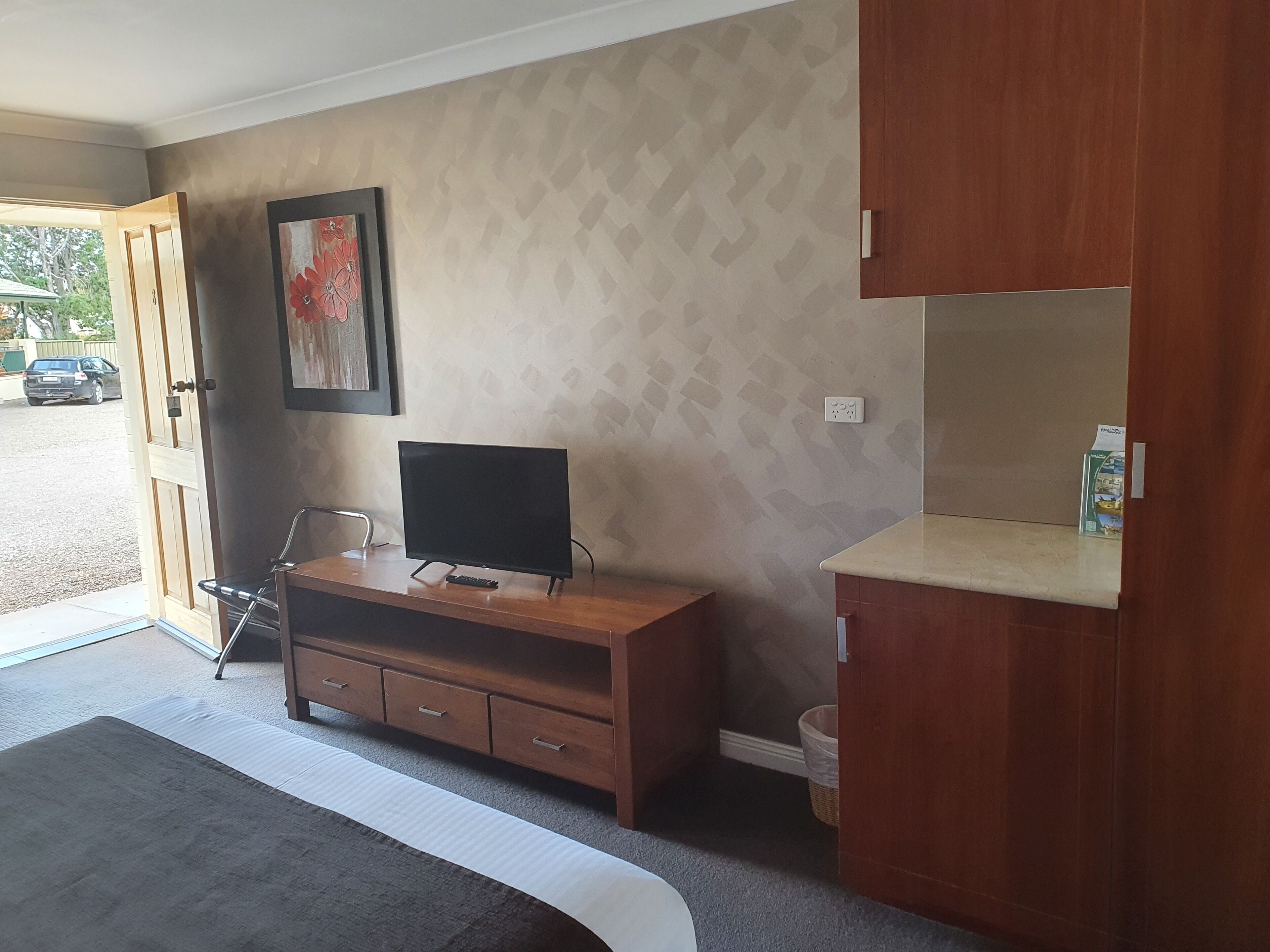 Quarto com uma escrivaninha de madeira, televisão e um quadro na parede.