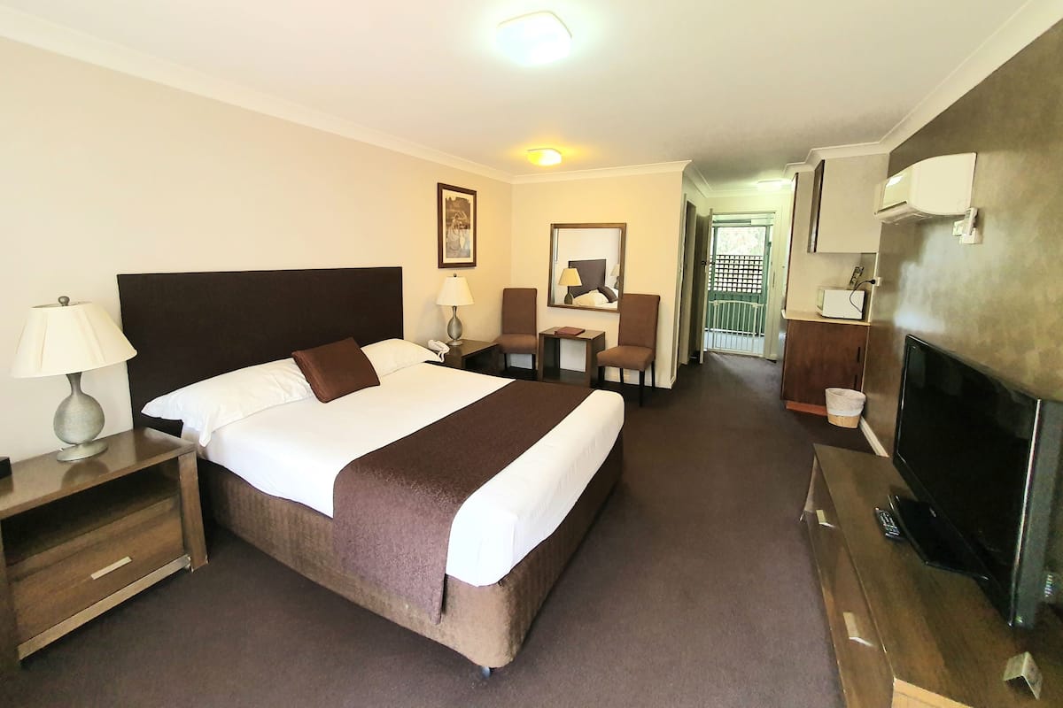 Quarto de hotel com uma cama grande, mesas de cabeceira, escrivaninha, cadeira, televisão e porta para uma varanda.