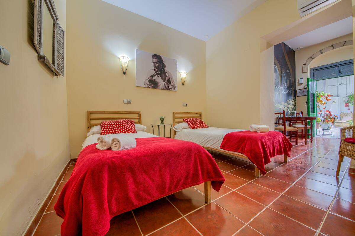 Quarto de hotel com duas camas, almofadas com bolinhas vermelhas e um cobertor vermelho.