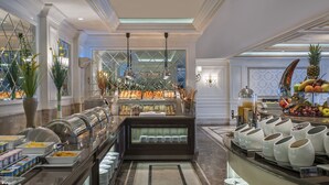 Uma área de buffet com diversas opções de comida, uma exposição de frutas e um espaço de estar com um tapete estampado.