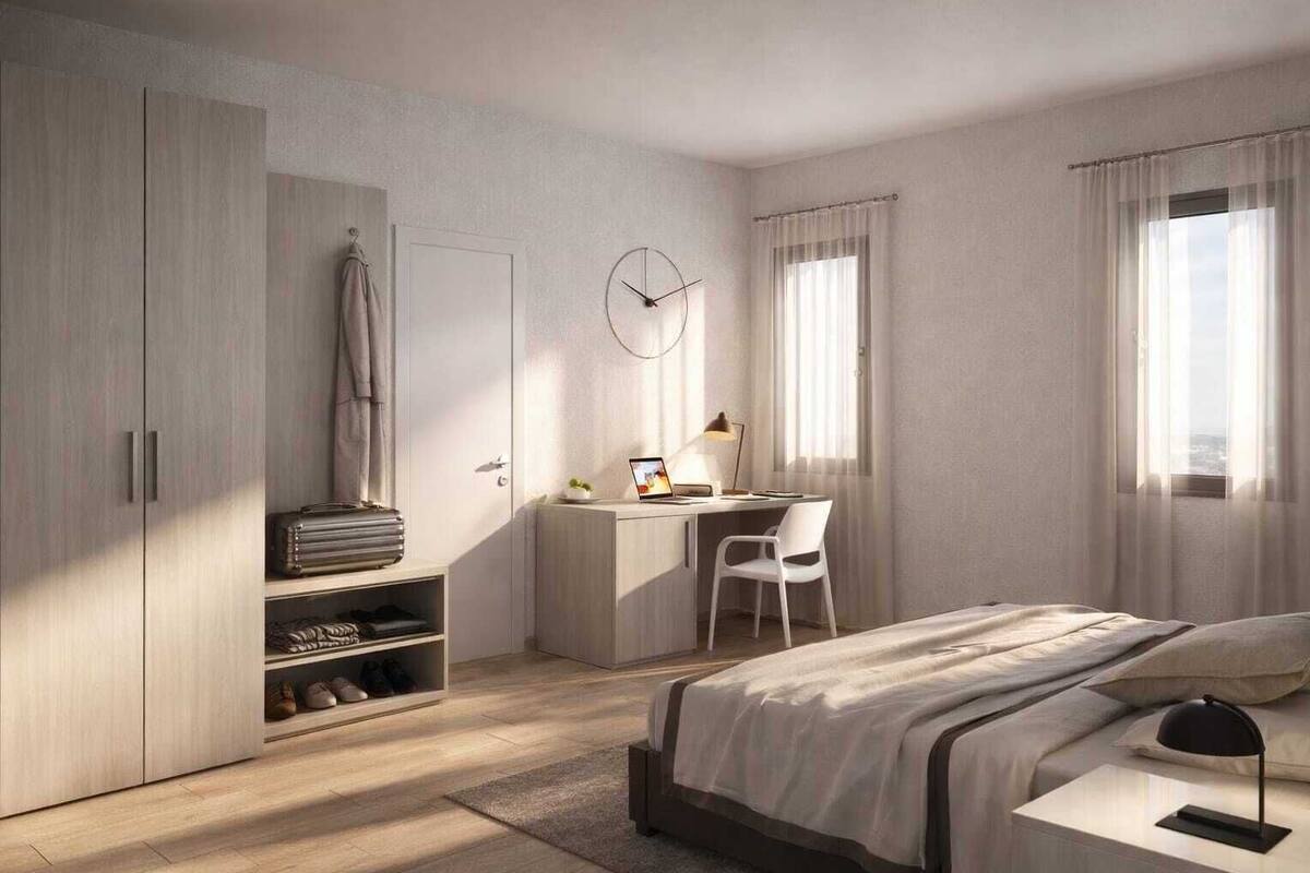Um quarto com cama, escrivaninha, cadeira, guarda-roupa e relógio na parede.