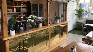 Uma área de bar com prateleiras de garrafas de bebidas, um balcão com flores e vista para o exterior através de uma janela.