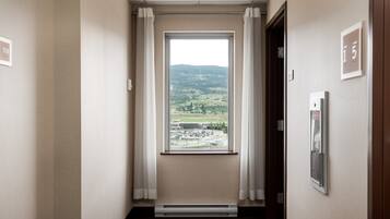 Corredor de hotel com uma janela grande que oferece vista para um estacionamento e colinas ao longe.