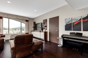 Uma sala de estar moderna com um piano, uma janela grande com vista para a cidade e um espaço de estar aconchegante.