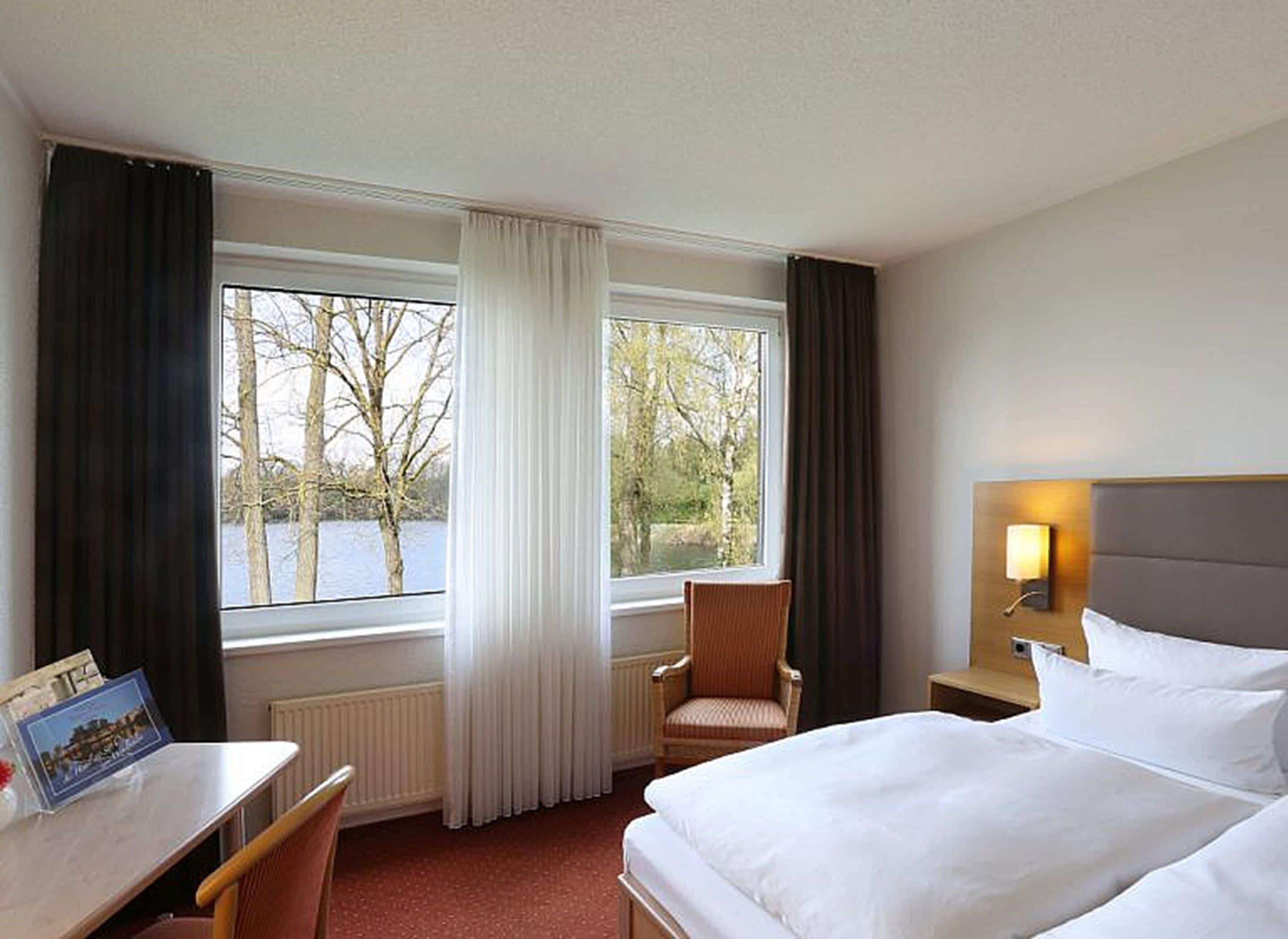 Quarto de hotel com cama, cadeira, mesa e janela com cortinas.