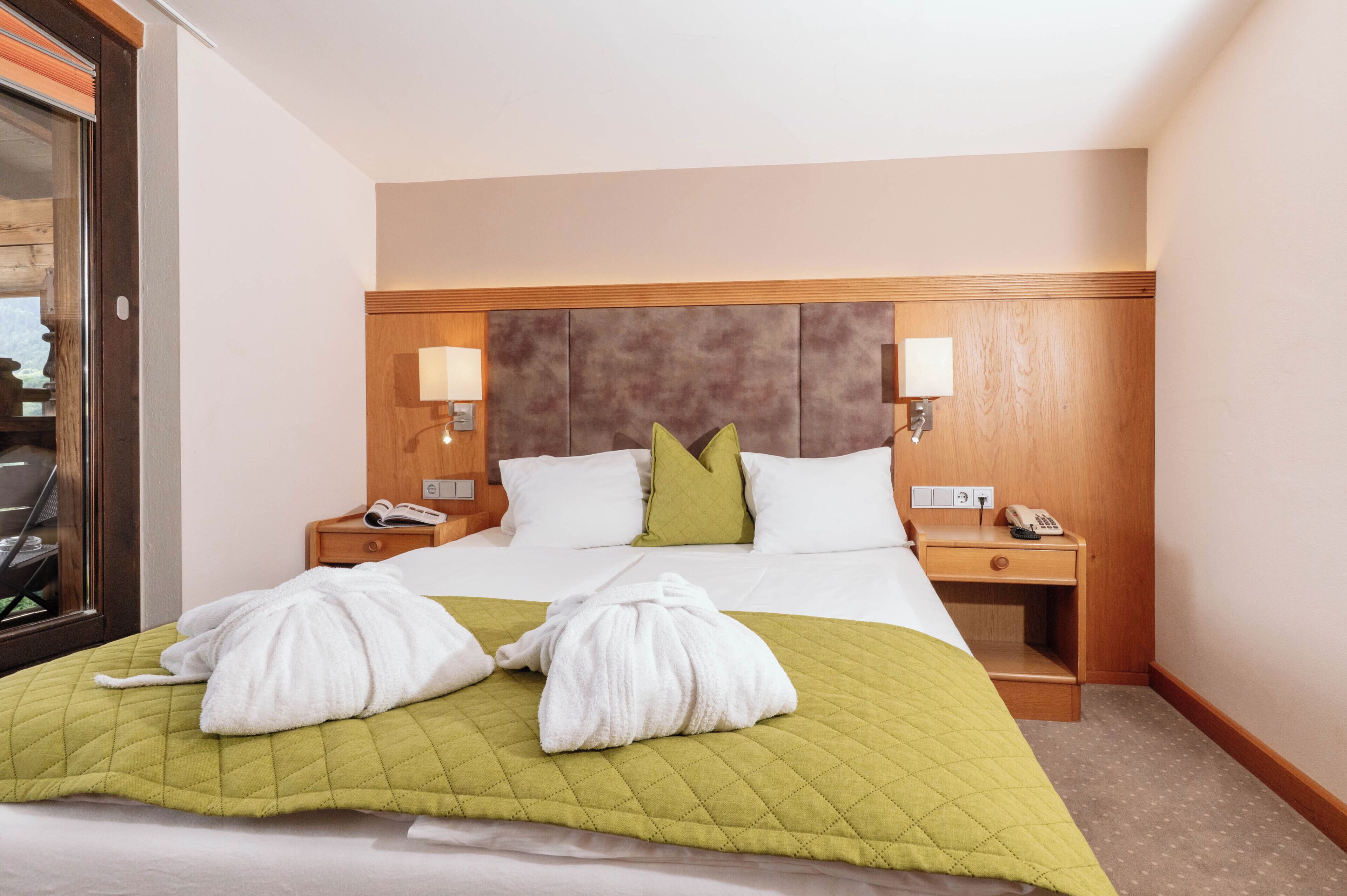 Quarto de hotel com uma cama, duas mesas de cabeceira, uma luminária e vista para o exterior.