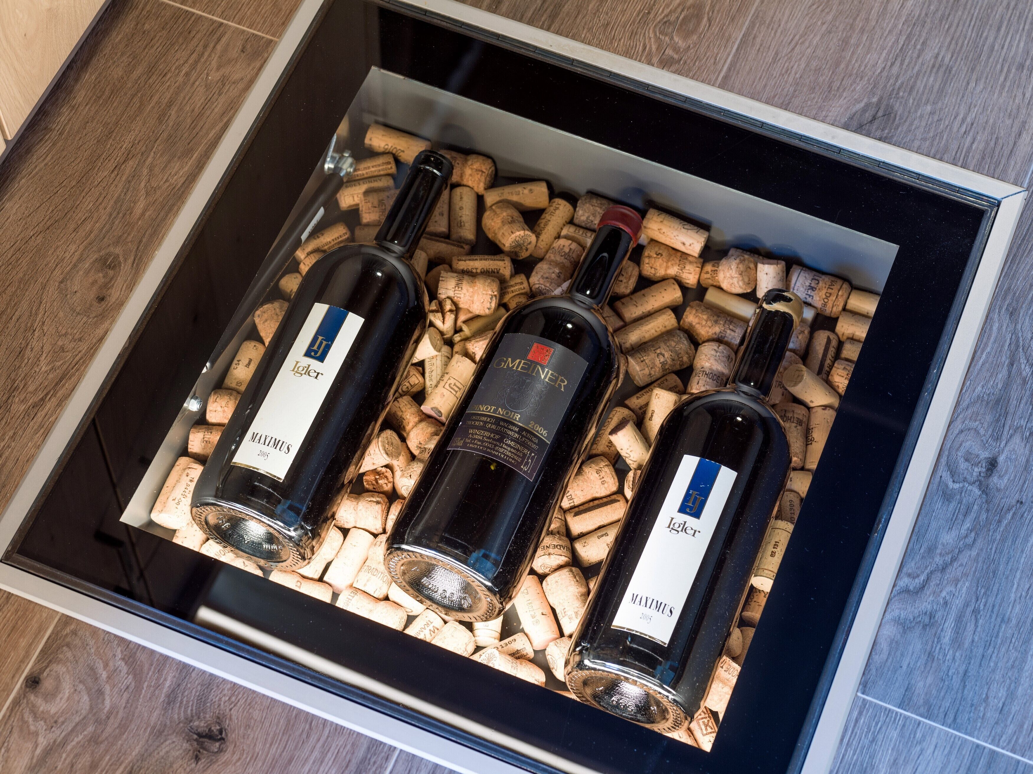 Uma gaveta com três garrafas de vinho e várias rolhas.