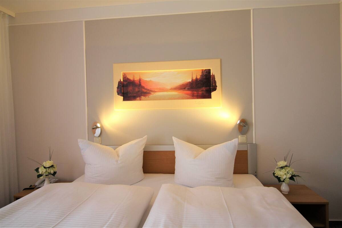 Quarto de hotel com uma cama grande, duas mesas de cabeceira e um quadro sobre a cama.