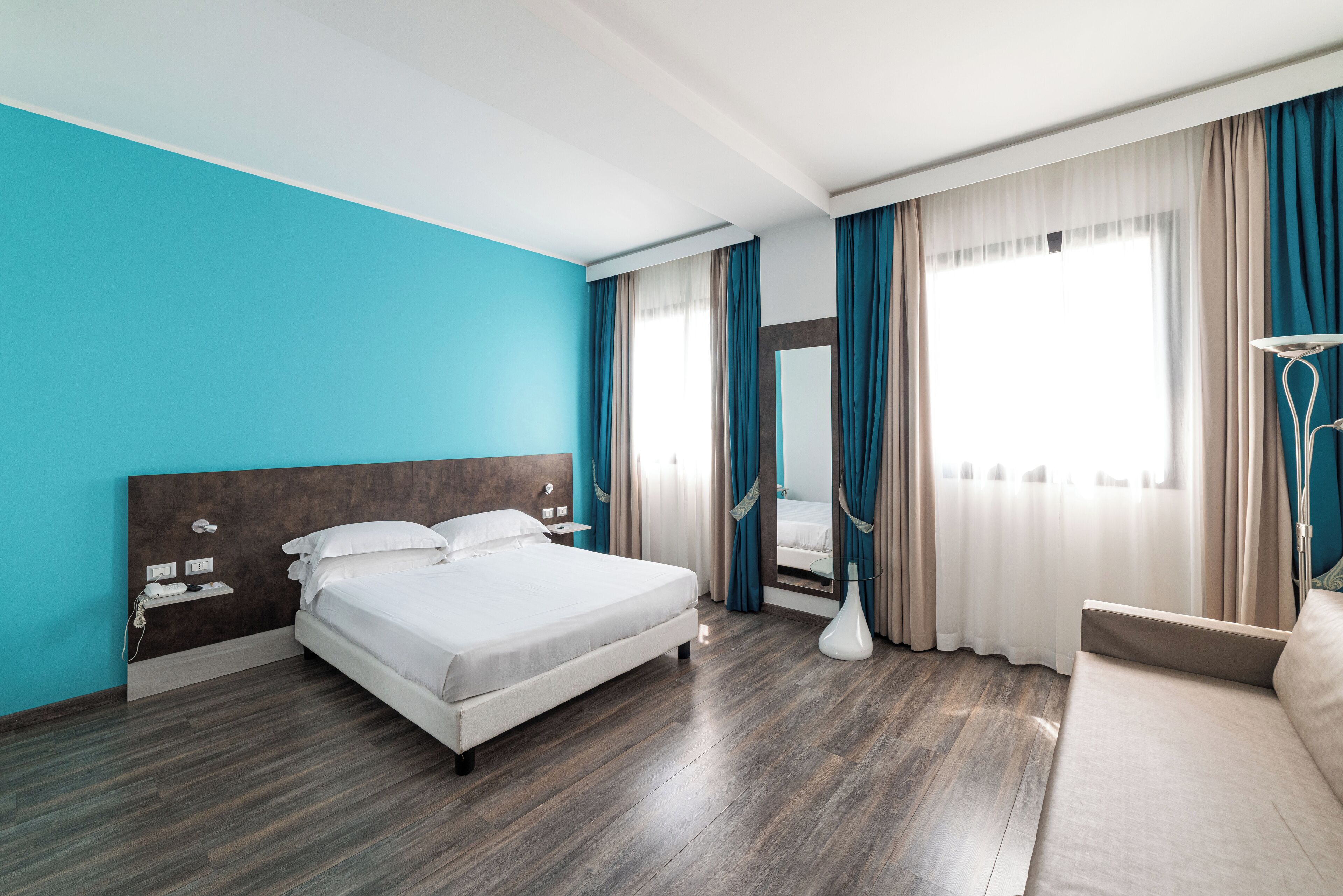 Quarto de hotel moderno com uma cama grande, um sofá e vista para a cidade.