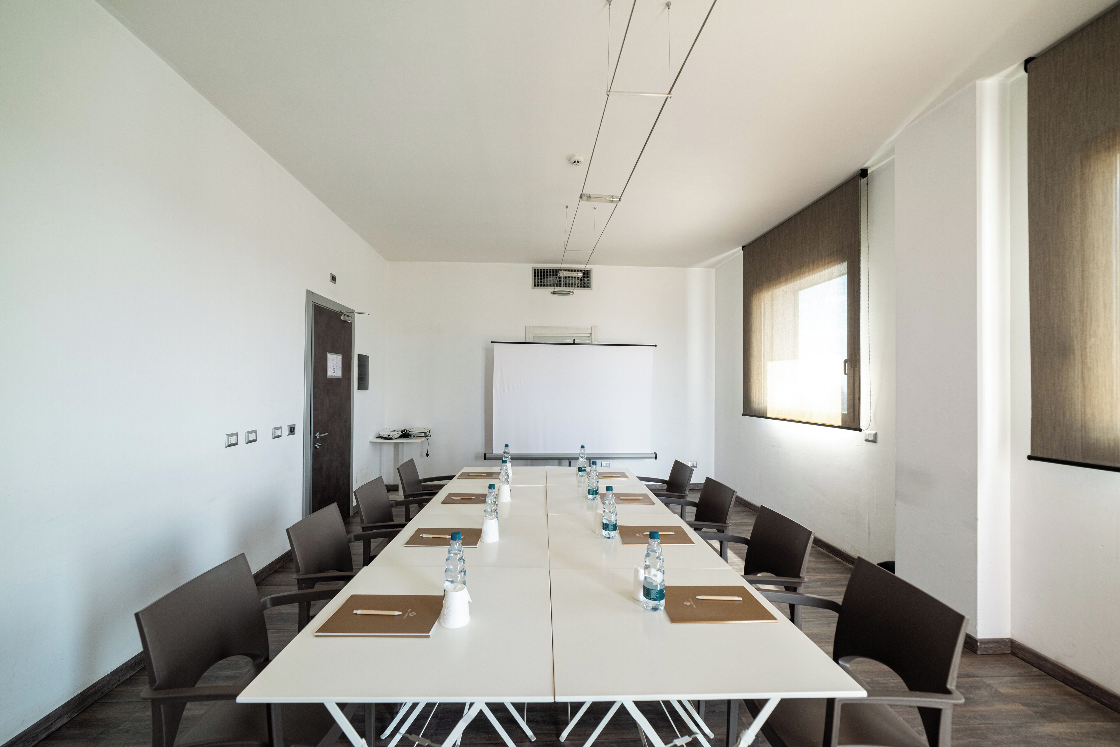 Uma sala de conferência com uma mesa comprida, cadeiras, garrafas de água e um quadro branco.