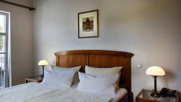 Quarto com cabeceira de madeira, duas mesas de cabeceira com abajures, cama com roupa de cama branca e um quadro na parede.