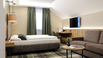 Quarto de hotel com cama, sofá, mesa pequena com um vaso, escrivaninha com computador e televisão na parede.
