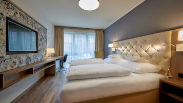 Quarto de hotel moderno com uma cama grande, uma TV presa a uma parede decorativa, uma escrivaninha com cadeira e uma janela com cortinas.