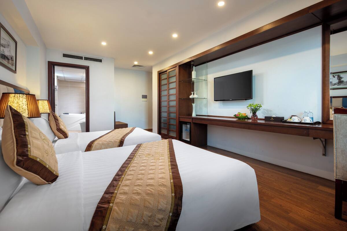 Quarto de hotel com duas camas, uma escrivaninha com televisão de tela plana e um espelho grande.