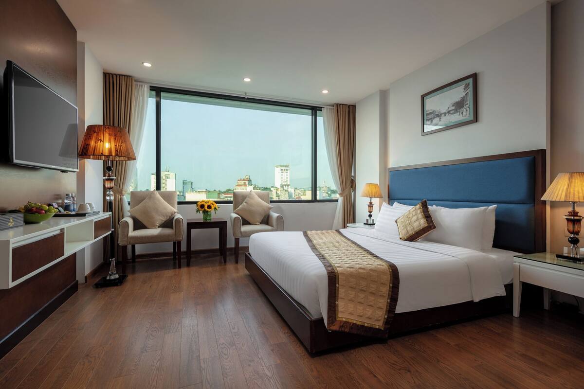 Quarto de hotel com uma cama grande, escrivaninha, cadeira, TV e vista para a cidade.