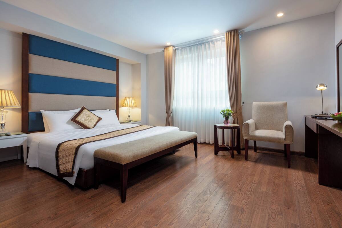 Quarto de hotel com uma cama grande, uma escrivaninha, uma cadeira e uma televisão.
