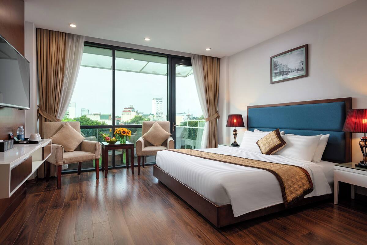 Quarto de hotel com uma cama grande, uma escrivaninha, uma cadeira, uma televisão e vista para a cidade.